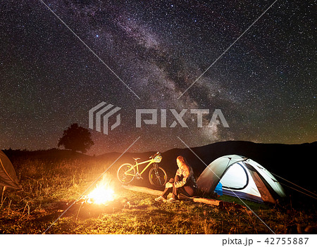 Woman resting at night camping near campfire, tourist tent, bicycle ...