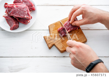 Closeup of the hands of a butcher cutting slices of raw meat off a ...