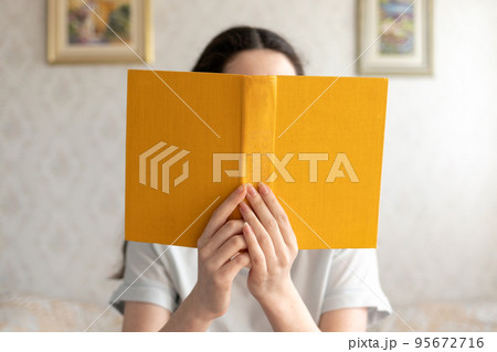 A young woman reads a book, hiding her face...の写真素材 [95672716] - PIXTA
