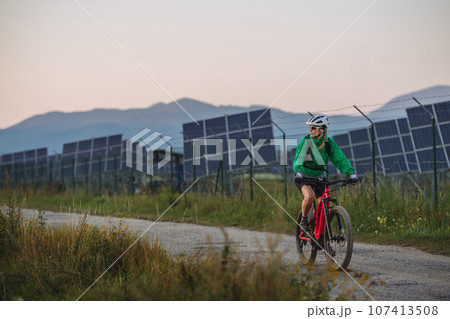 Female cyclist riding in front of solar panels...の写真素材 [107413508] - PIXTA