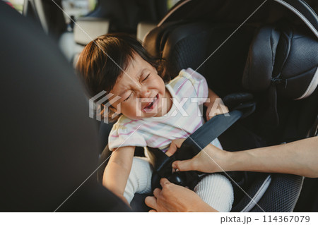 mother is fastening safety belt to crying toddler girl in car seat ...