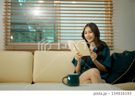 Woman reading book while resting on sofa at homeの写真素材 [134916193] - PIXTA